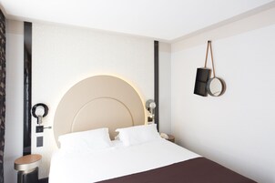 Quarto de hotel moderno com uma cama grande, mesas de cabeceira, um espelho redondo e uma pequena mesa redonda.