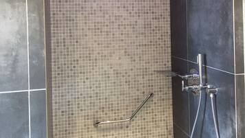 Uma área de chuveiro moderna com parede revestida de azulejos, chuveiro manual e torneira fixada na parede.