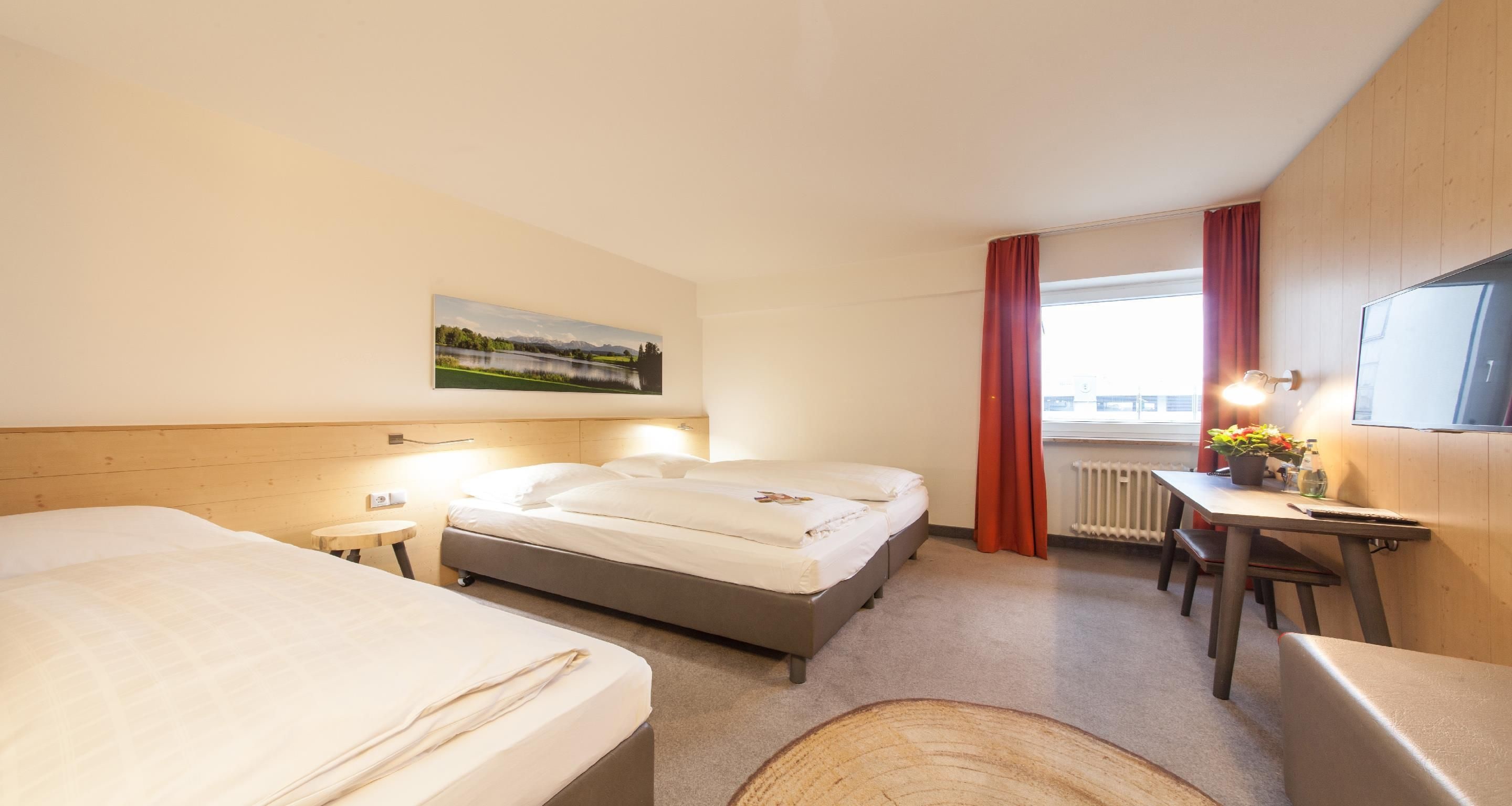 Quarto de hotel com duas camas, uma escrivaninha, uma cadeira, uma janela com cortinas, um quadro na parede e um radiador.
