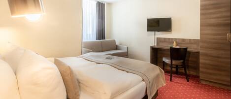 Quarto de hotel com uma cama, escrivaninha, cadeira, televisão e guarda-roupa.