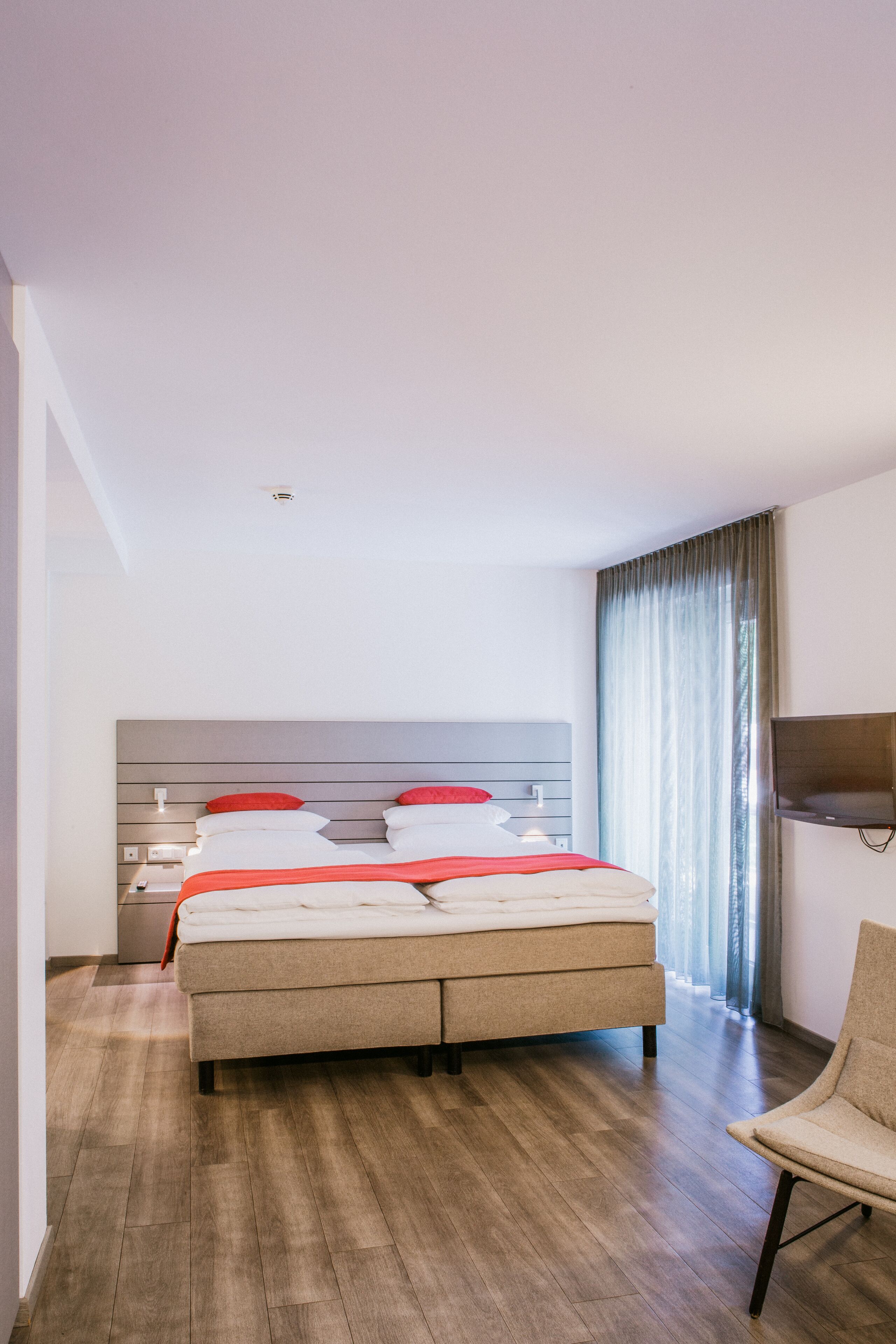 Quarto de hotel com uma cama grande, televisão na parede e uma cadeira.