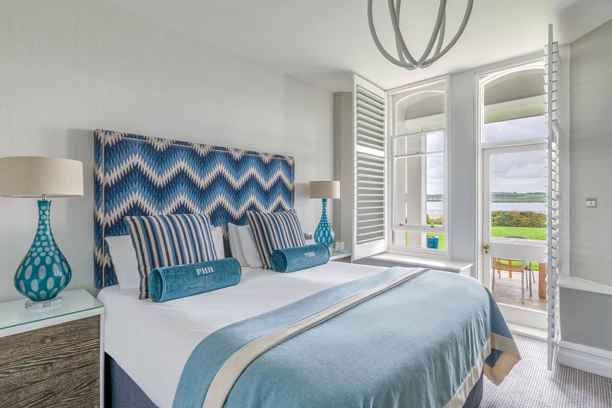 Quarto com uma cama grande, duas mesas de cabeceira, vista para o exterior por uma janela e um lustre no teto.