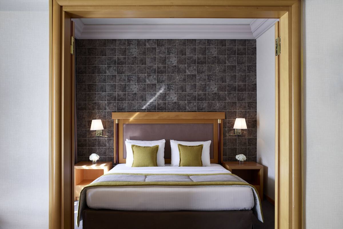 Quarto de hotel com uma cama grande, duas mesas de cabeceira e uma parede revestida de azulejos escuros.