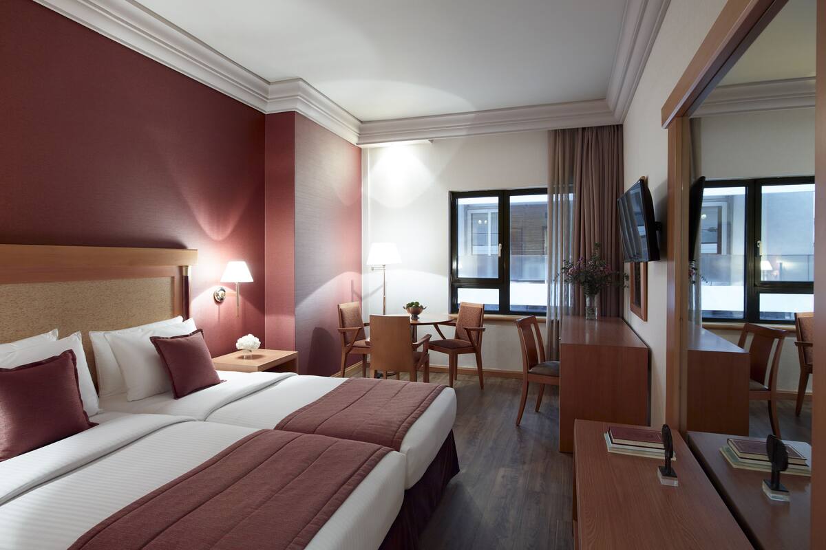 Quarto de hotel com uma cama grande, uma escrivaninha, uma cadeira, uma televisão e uma janela com cortinas.