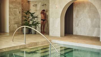 Uma área de piscina interior moderna com barreira de vidro, espaço para chuveiro e um vaso de planta.
