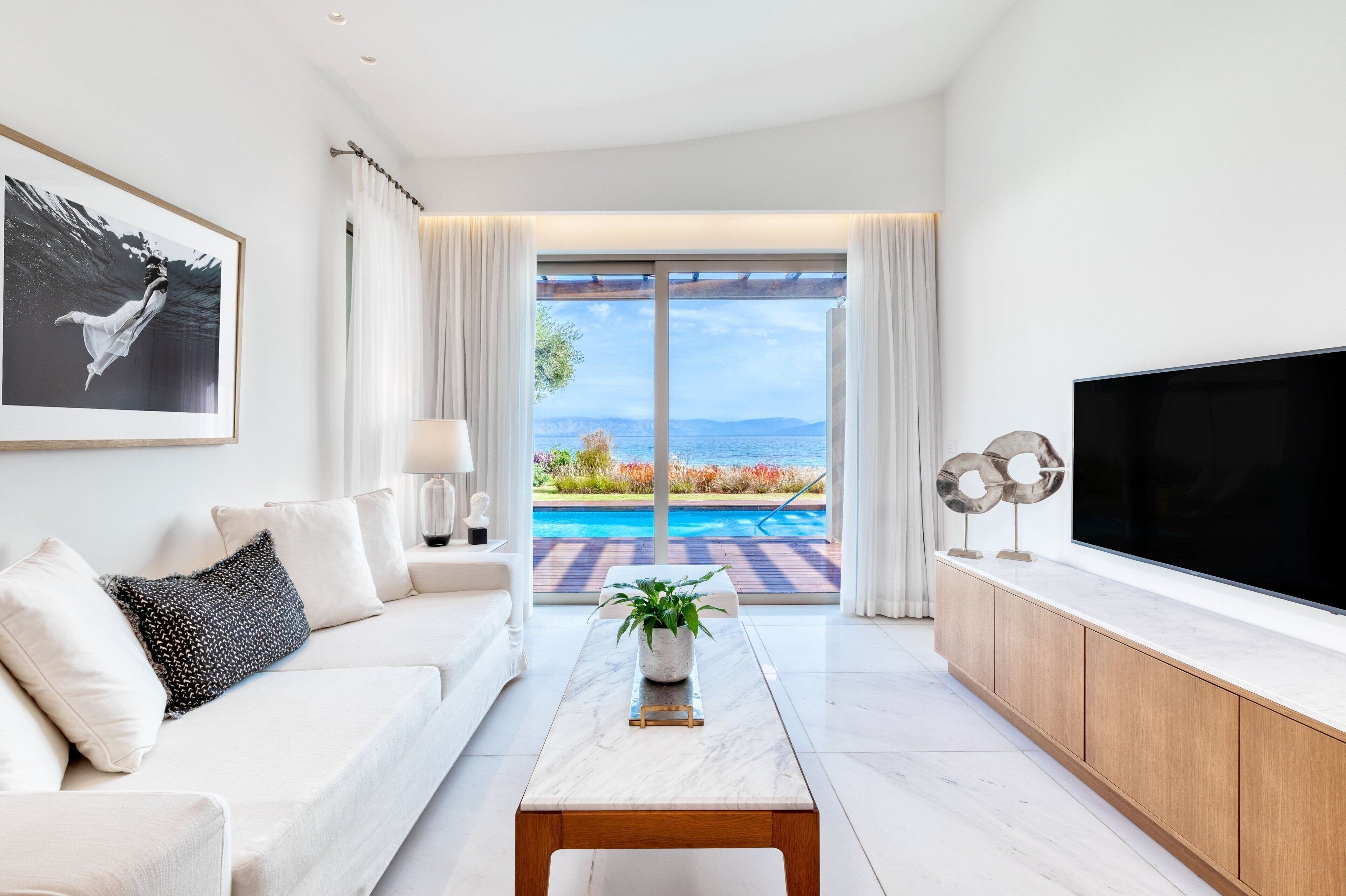 Sala de estar moderna com televisão grande, sofá, mesa de centro e vista para piscina e oceano.