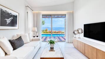 Sala de estar moderna com televisão grande, sofá, mesa de centro e vista para piscina e oceano.