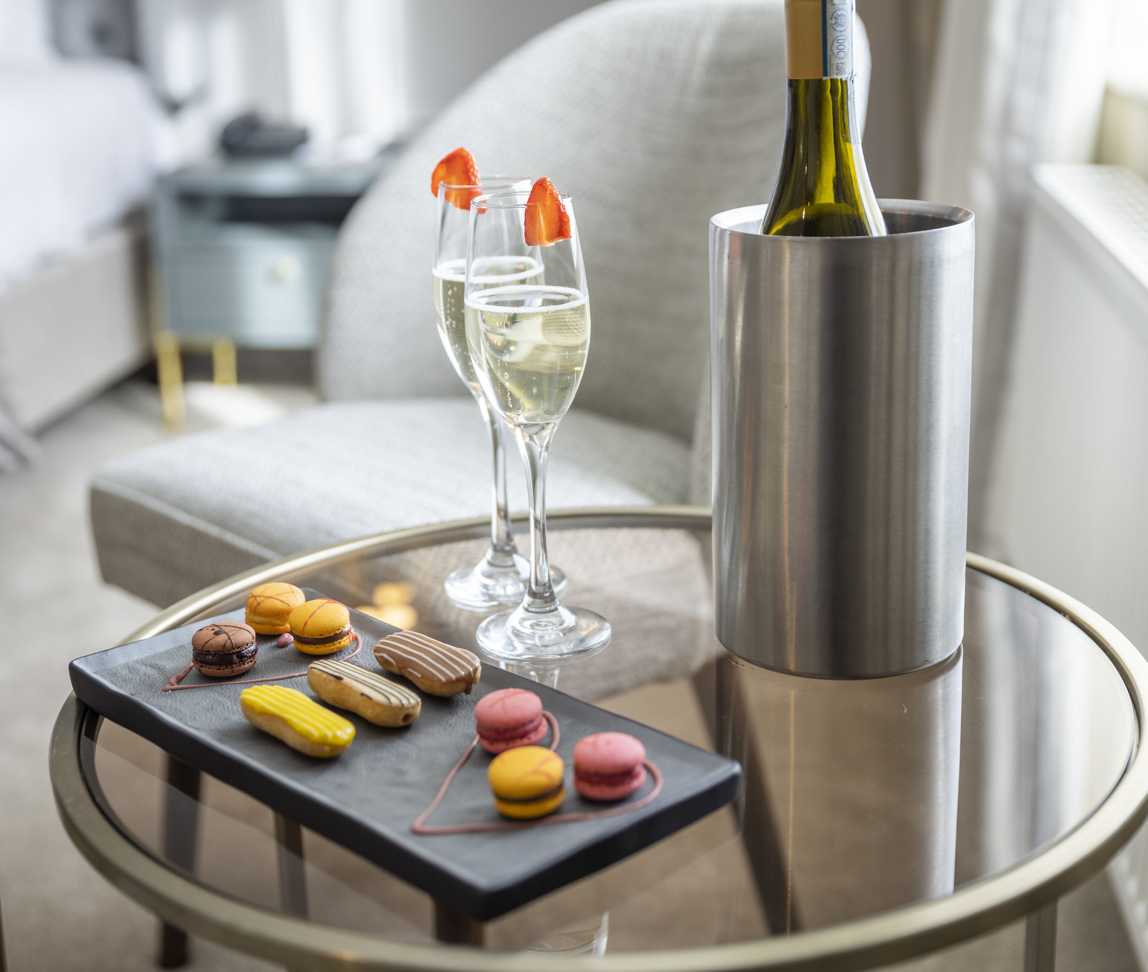 Uma mesa com uma garrafa de champanhe, copos e macarons.