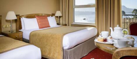 Quarto de hotel com duas camas, uma mesa de jantar com chá e vista para um lago.