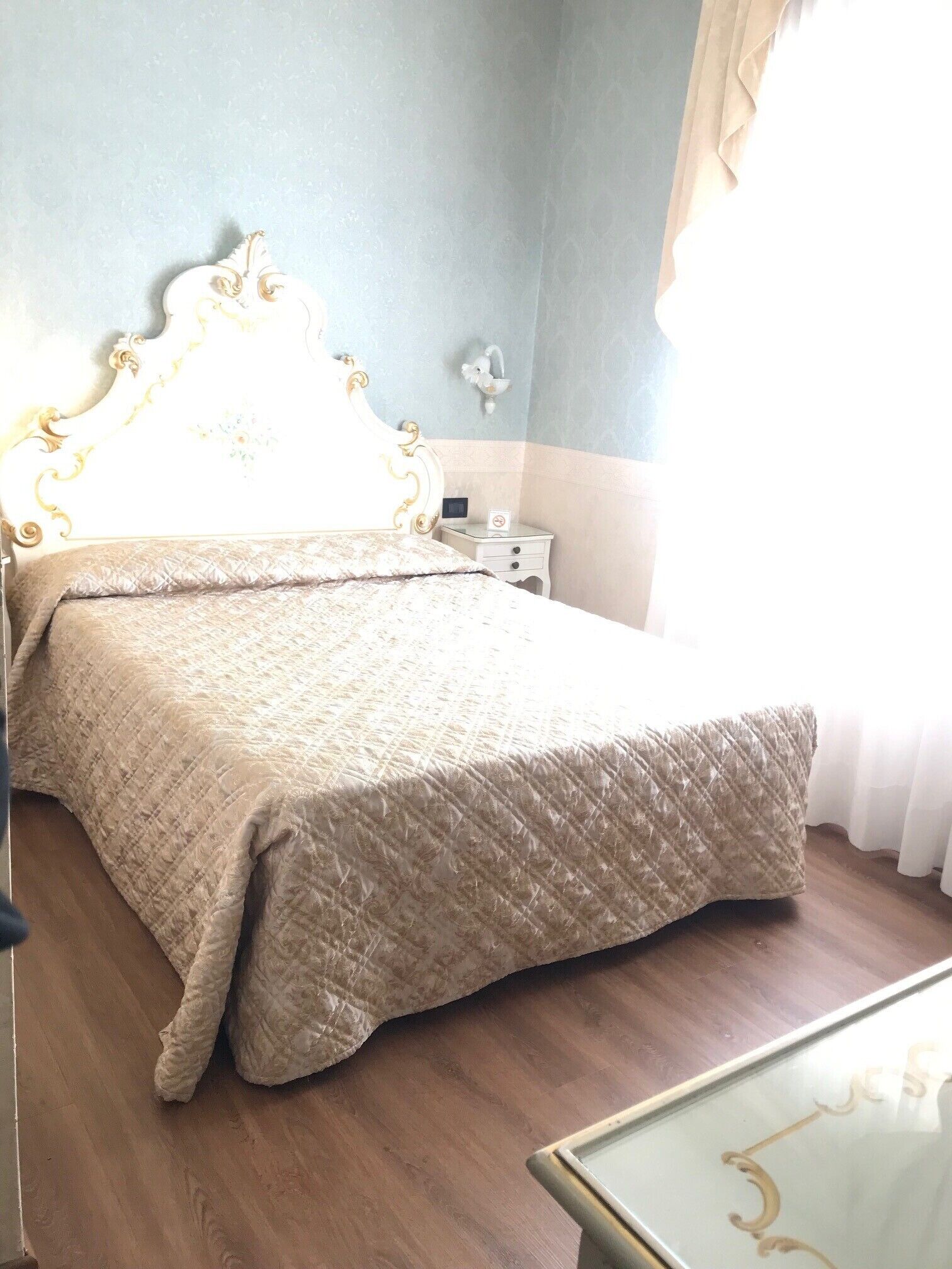 Quarto com uma cama grande, mesa de cabeceira e luminária fixada na parede.