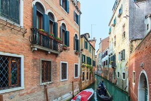 Um canal veneziano estreito ladeado por edifícios históricos com janelas em arco e sacadas.