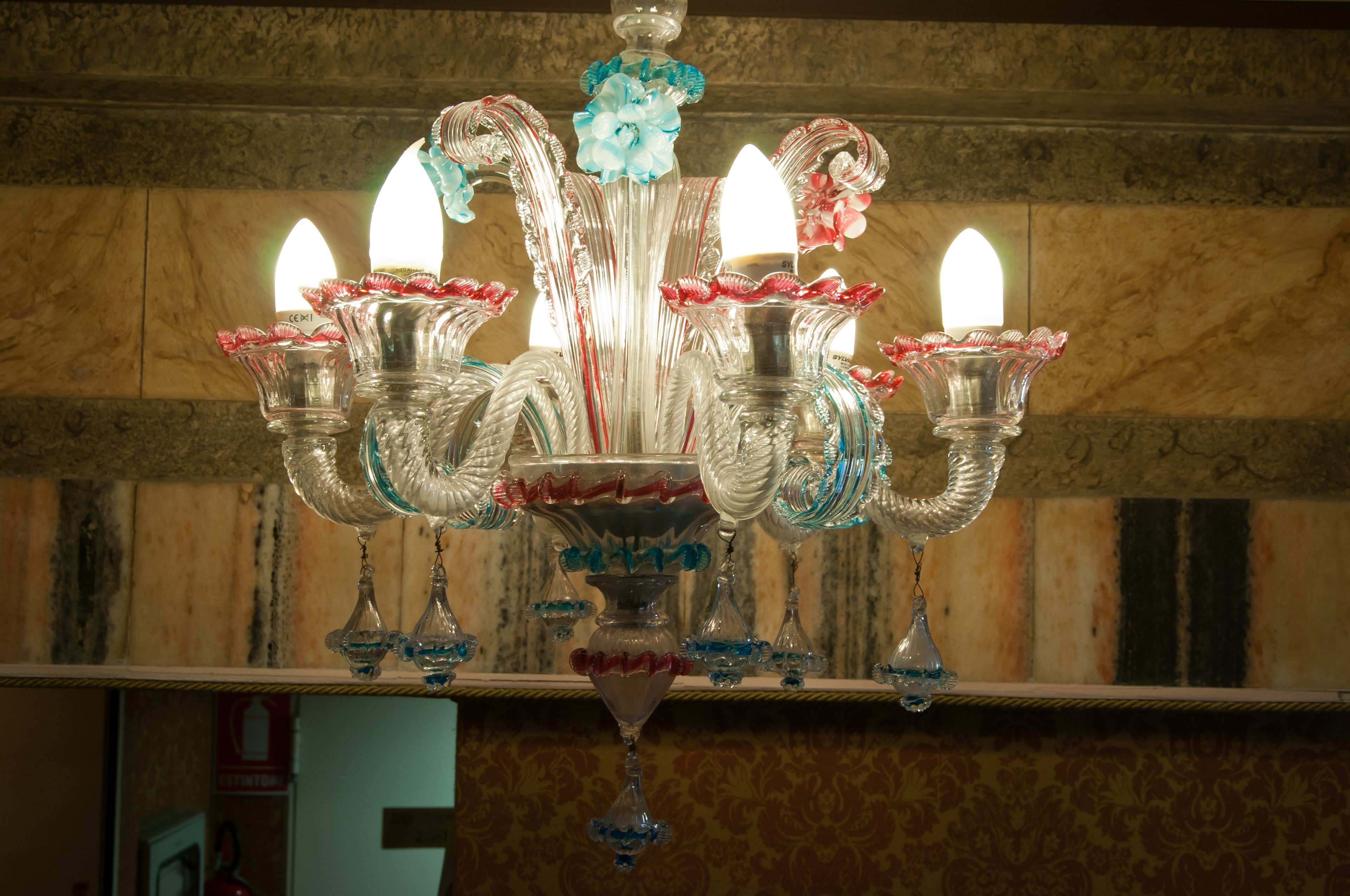 Um candelabro com vários braços e luzes semelhantes a velas, em frente a uma parede com padrão.