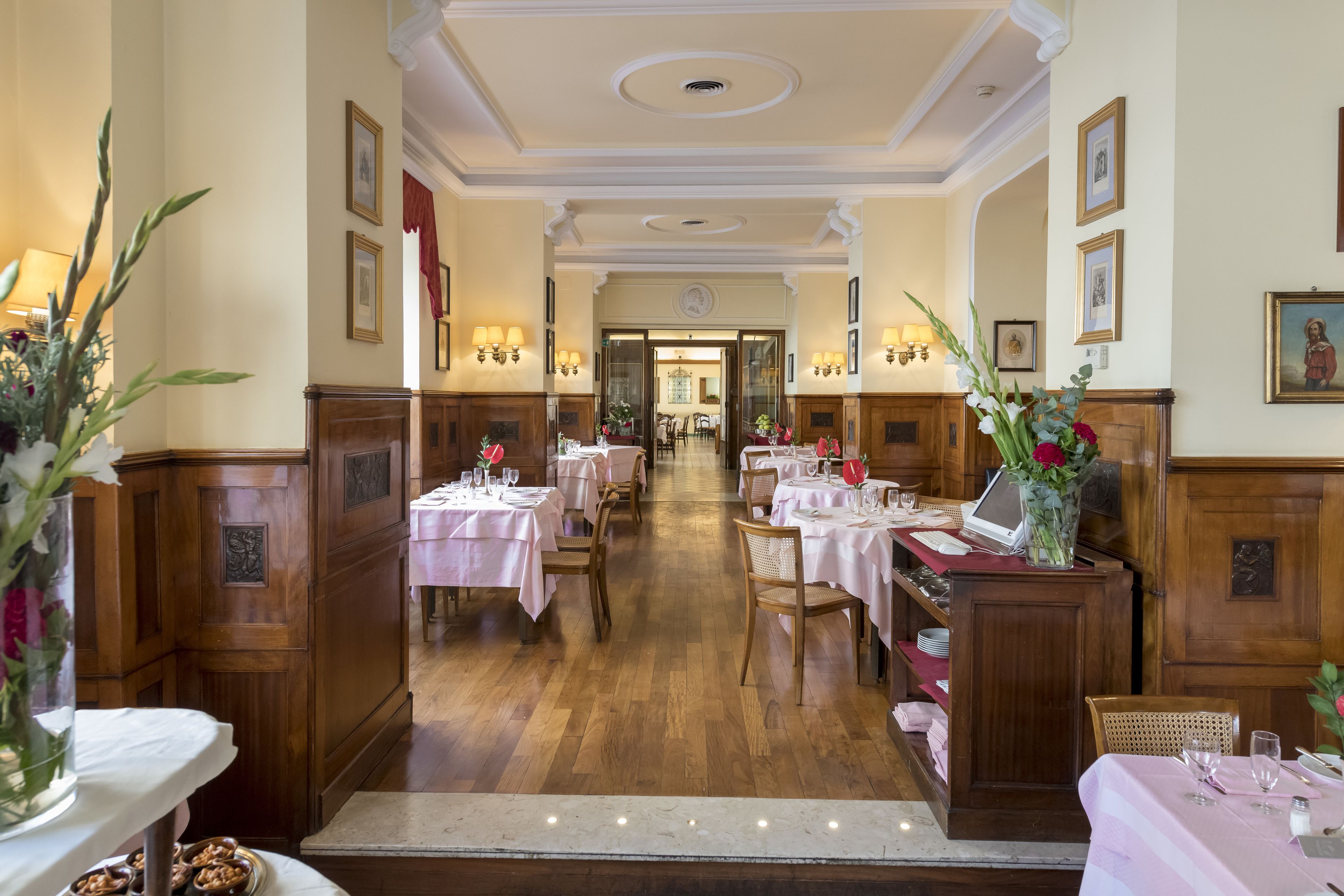 Restaurante com painéis de madeira, toalhas brancas e arranjos florais.