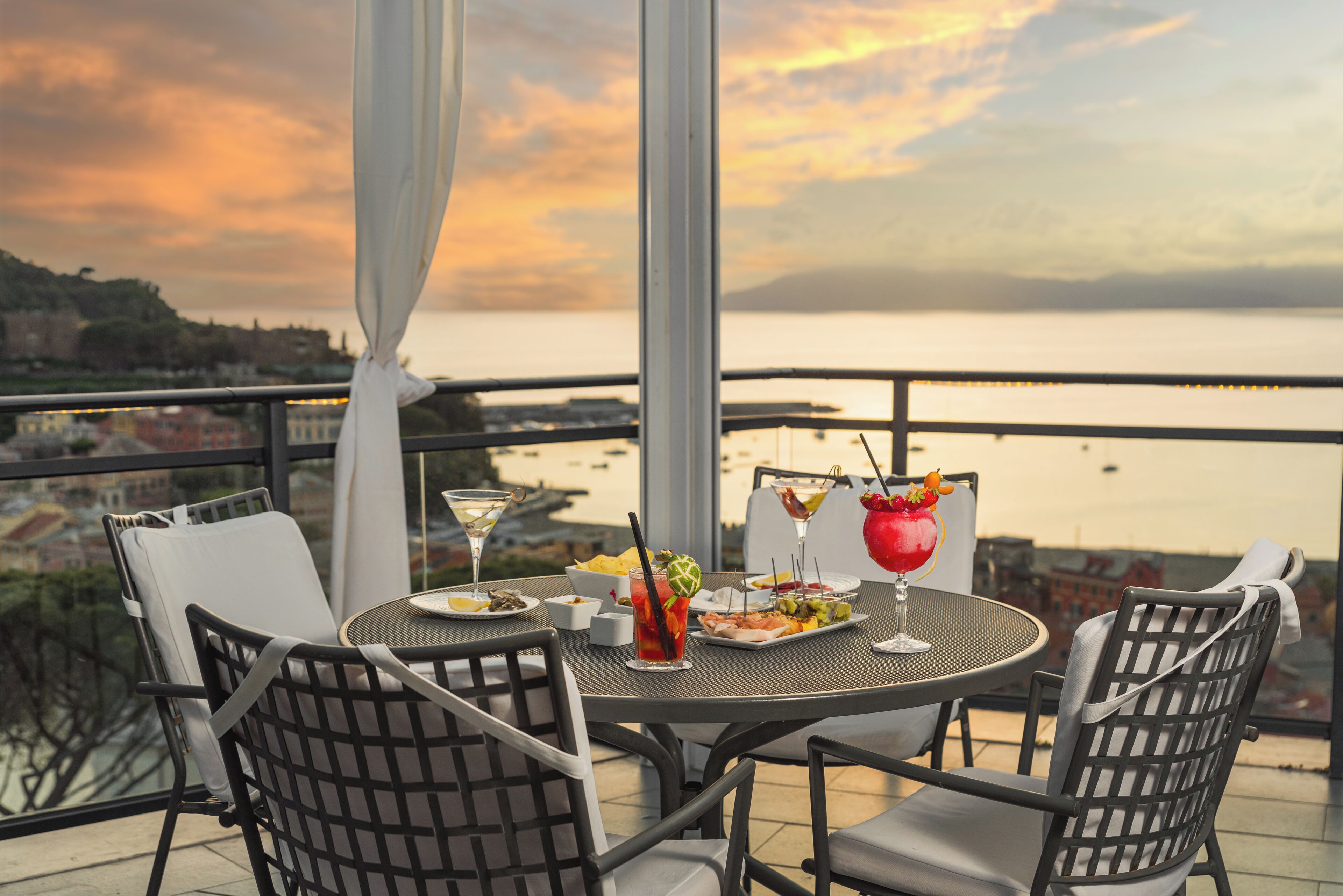 Mesa de jantar com cadeiras, um coquetel e vista para o mar e a paisagem urbana.