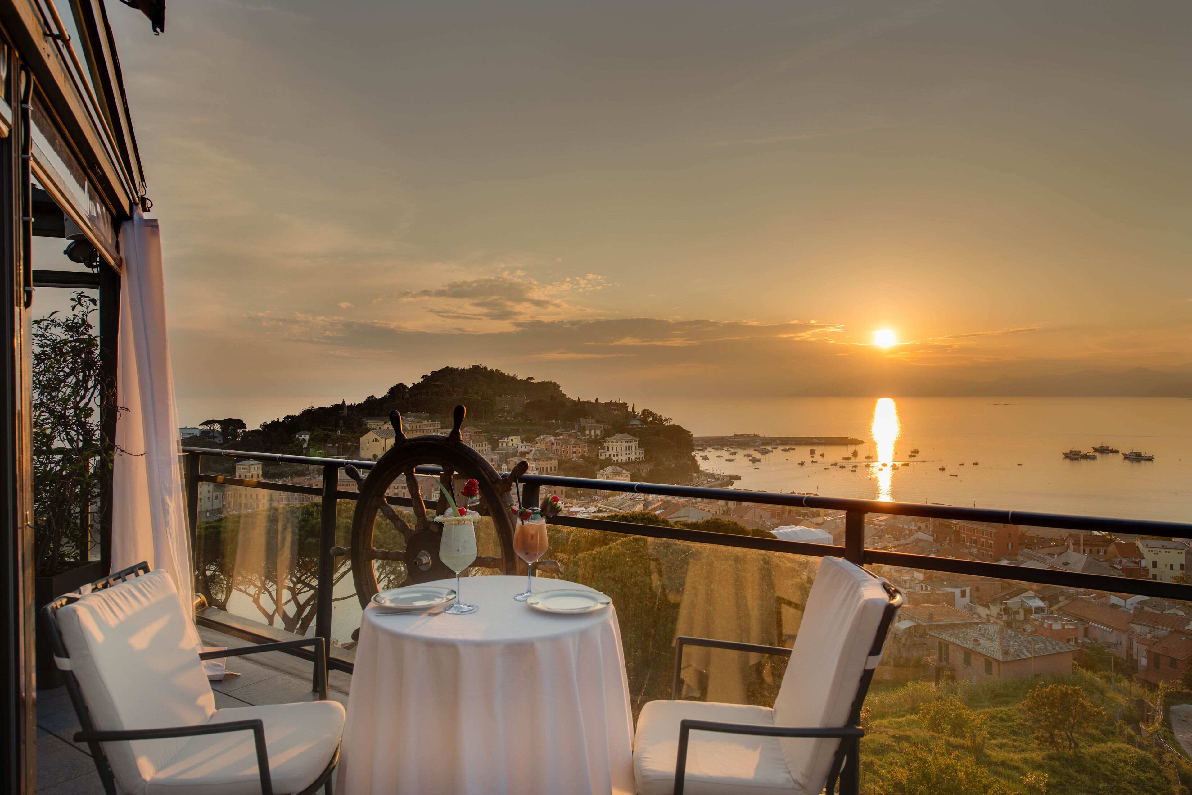 Mesa posta para dois, com vista para o pôr do sol sobre a água.