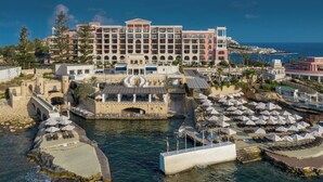 Um hotel à beira-mar com um edifício amplo, um porto de iates e um molhe rochoso com guarda-sóis.