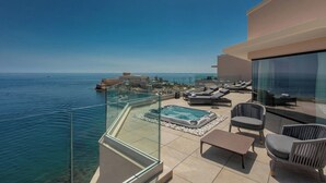 Terraço no telhado com guarda-corpo de vidro, hidromassagem, cadeiras de descanso e vista para o mar e uma ilha distante.