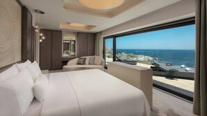 Quarto de hotel moderno com uma cama grande, área de estar e varanda com vista para o mar.