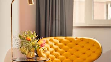 Um quarto com uma poltrona amarela estofada, uma pequena mesa redonda com um vaso de flores e um abajur.