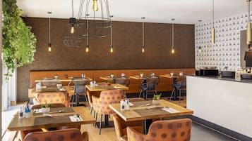 Restaurante com mesas de madeira e cadeiras estampadas, luminárias pendentes e parede decorada.