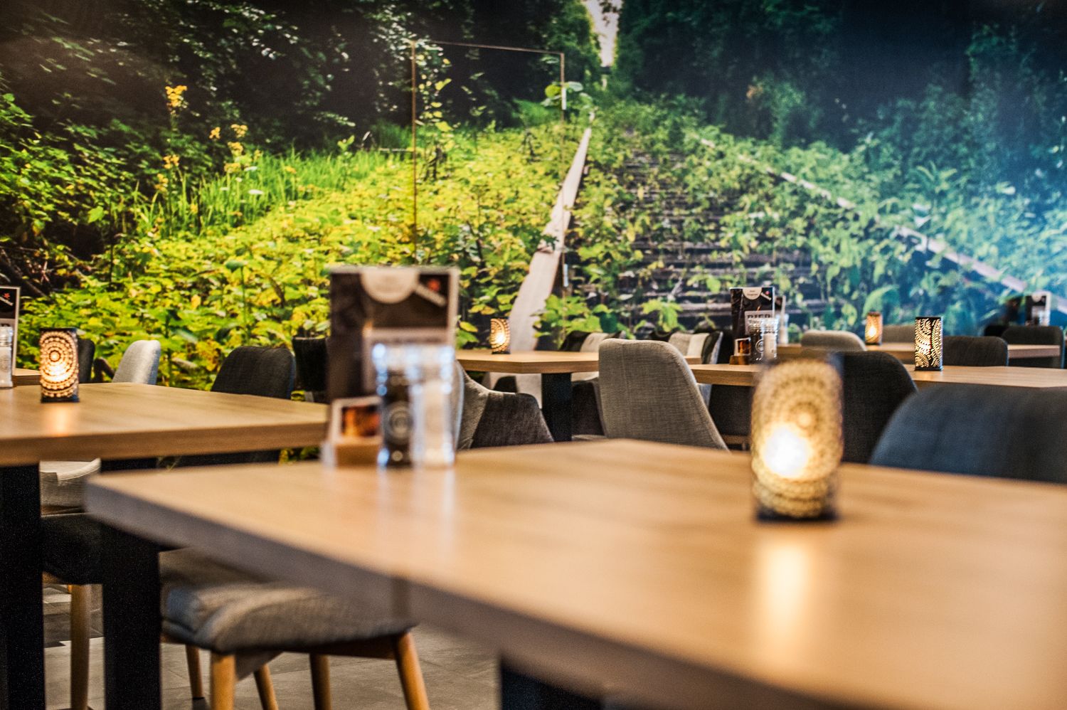 Um restaurante com mesas e cadeiras de madeira, um suporte para cardápio e castiçais decorativos.