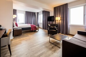Quarto de hotel com cama, escrivaninha, cadeira, sofá, televisão e janela com cortinas.