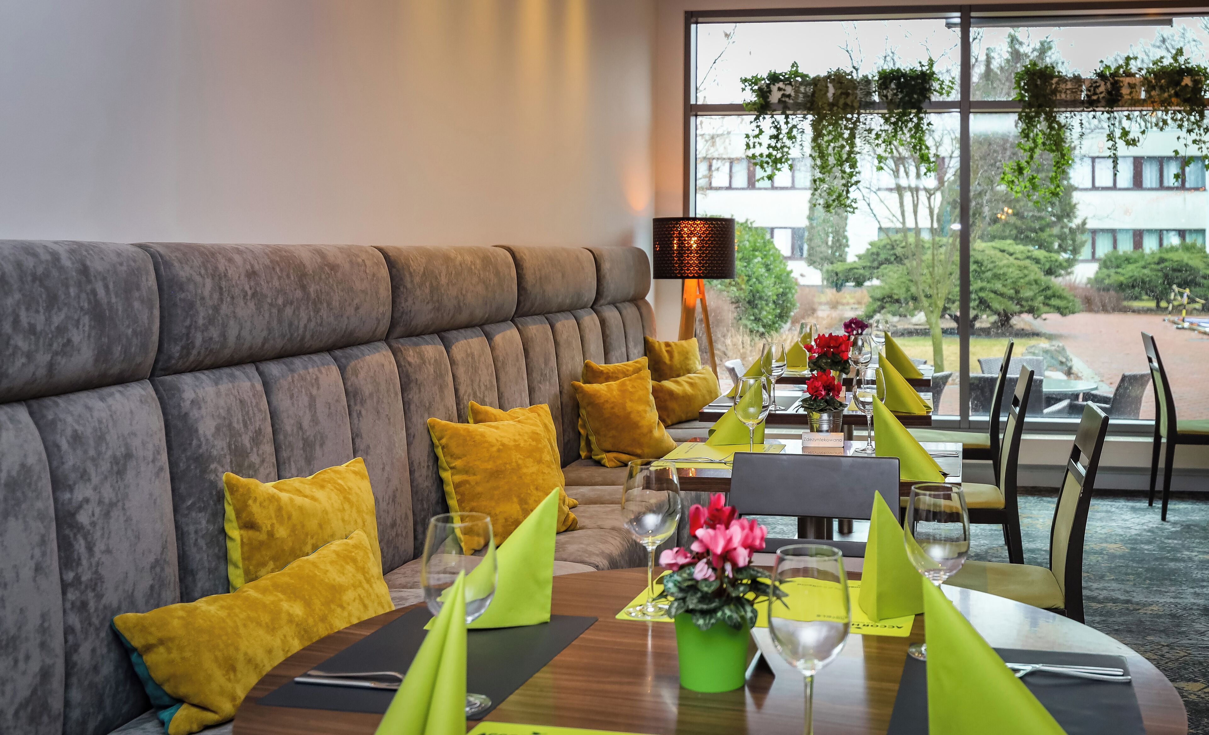 Restaurante com uma mesa de jantar comprida posta para uma refeição, um banco acolchoado e vista para o exterior.