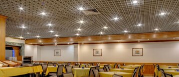 Uma sala de conferências com mesas e cadeiras, teto com padrão quadriculado e obras de arte emolduradas nas paredes.