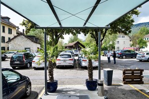 Uma área de estacionamento coberta com carros, plantas em vasos e um banco de madeira.