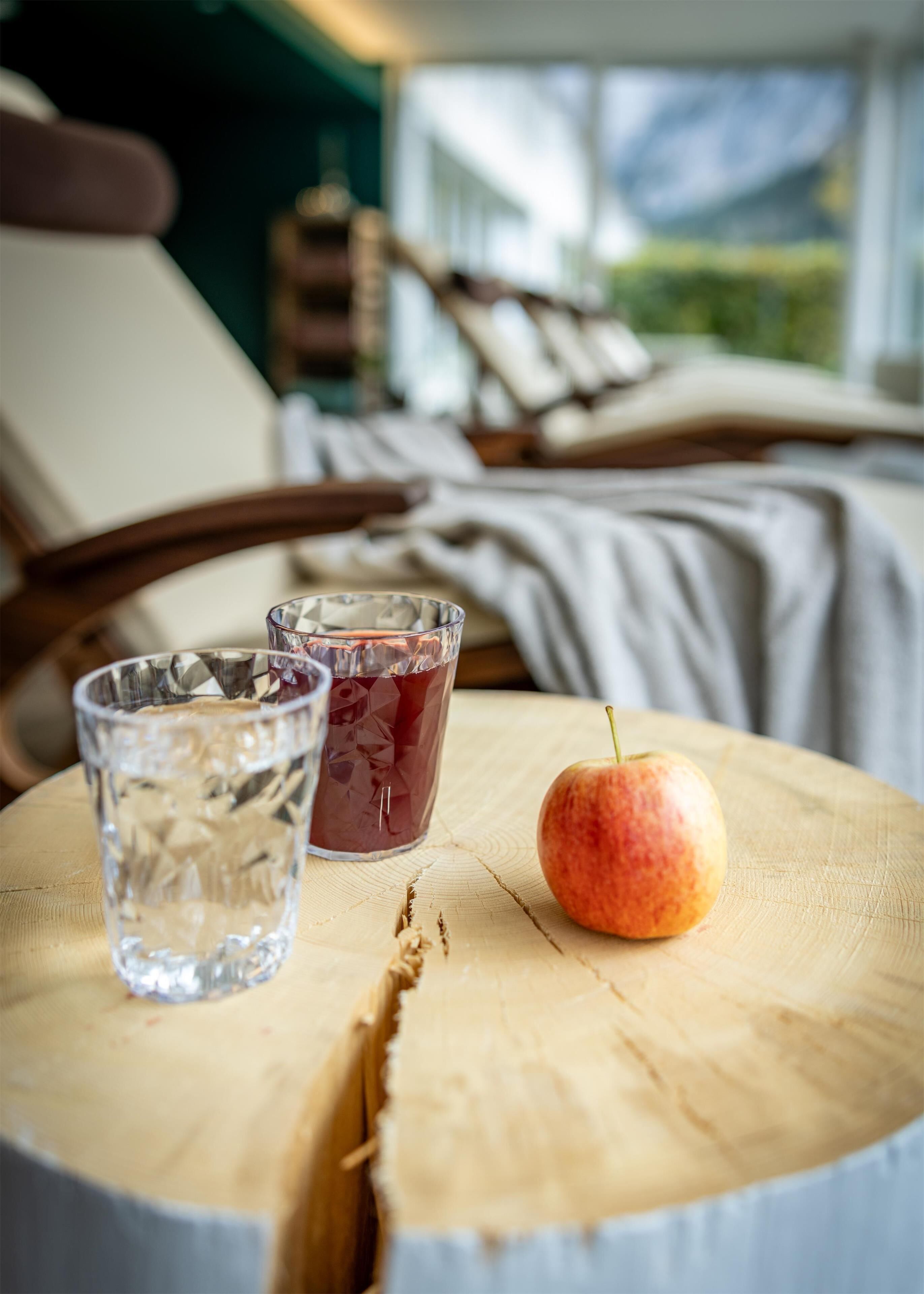 Uma mesa de madeira com dois copos de água e um copo de suco, e uma maçã sobre a superfície de madeira.