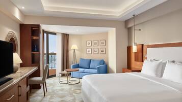 Quarto de hotel com uma cama, escrivaninha, cadeira, mesa pequena, sofá e televisão.