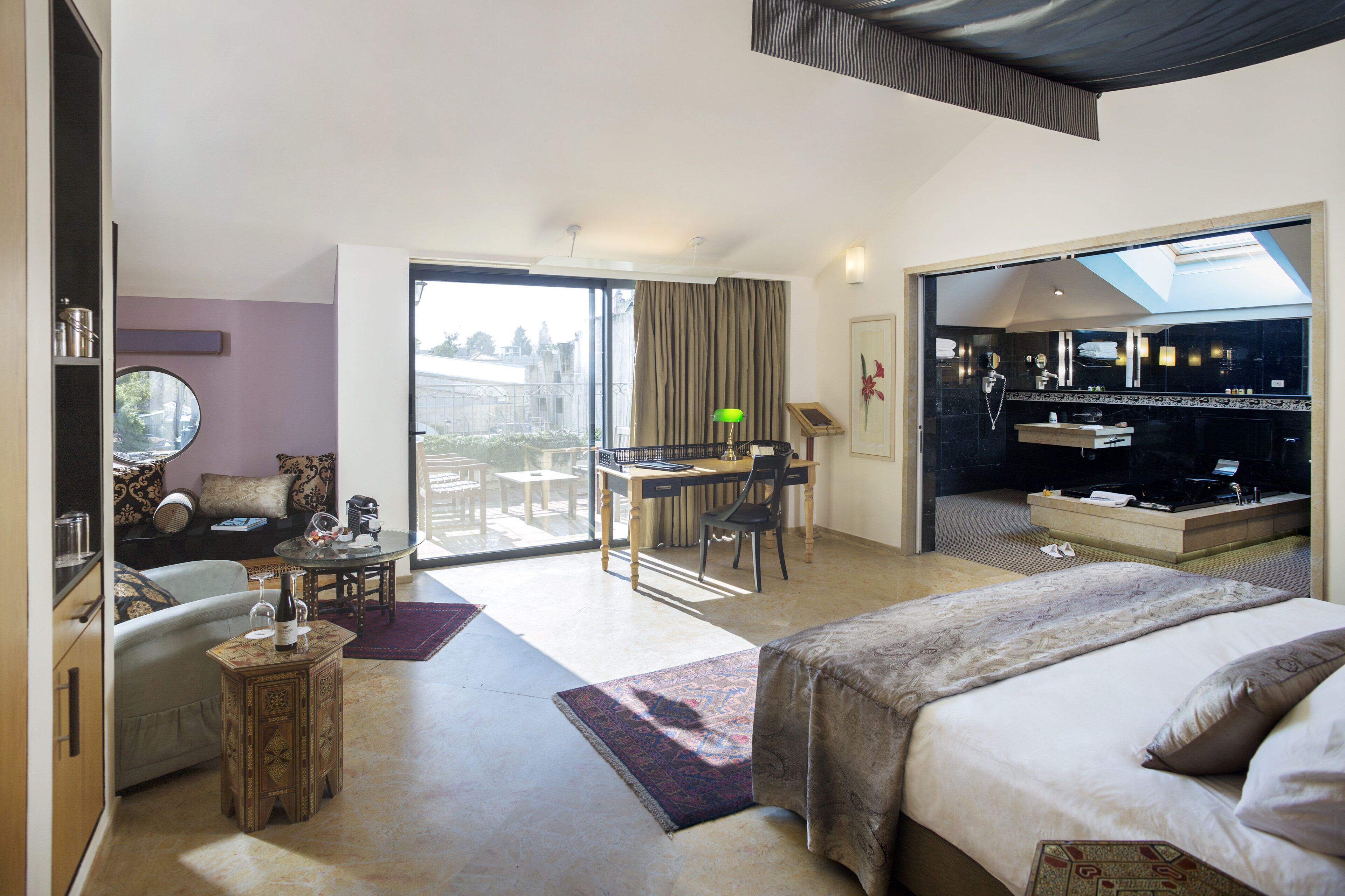 Quarto de hotel com cama, escrivaninha, poltrona, sofá e varanda com vista.