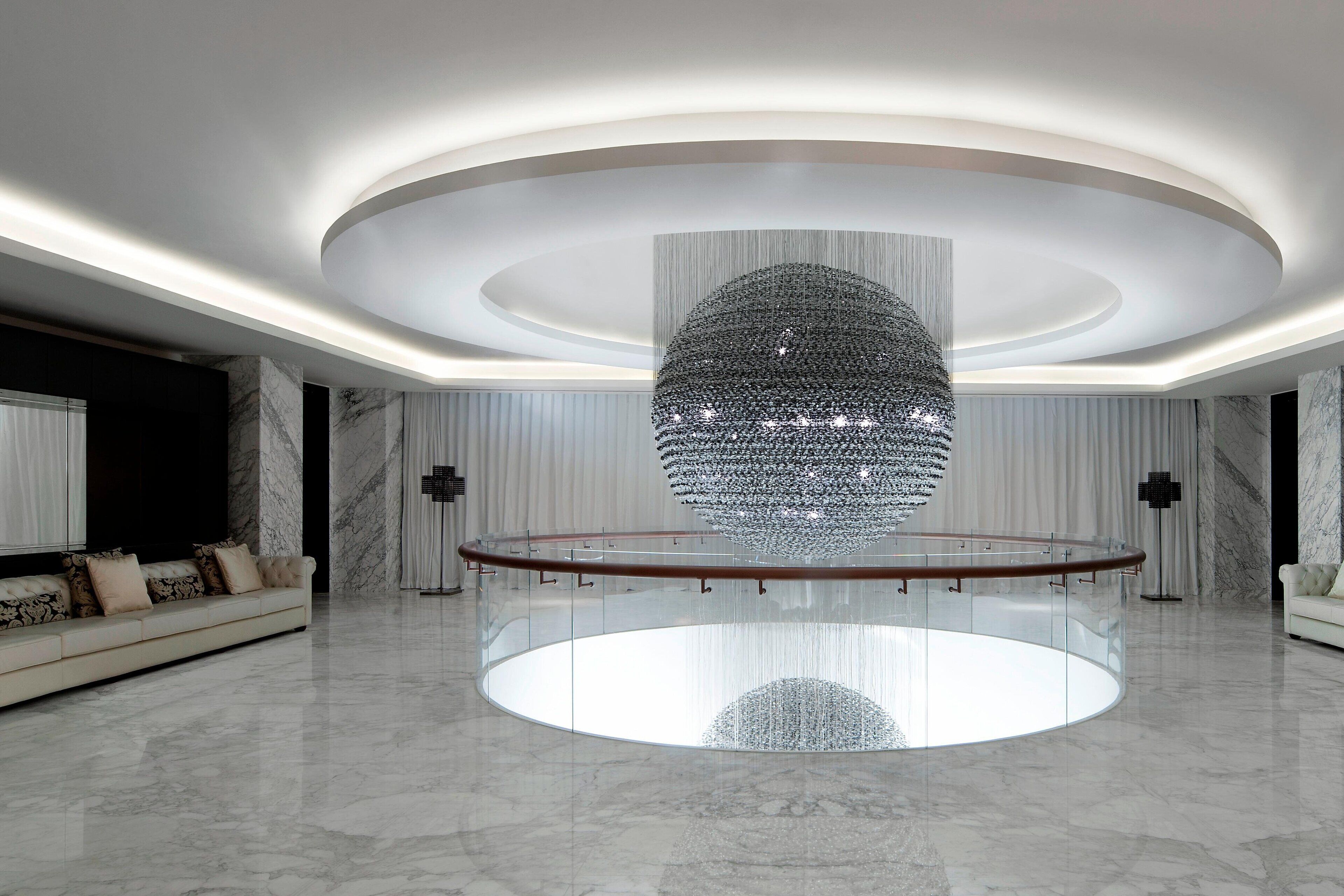 Um hall moderno com piso de vidro circular, um candelabro central e um sofá ao longo das paredes.