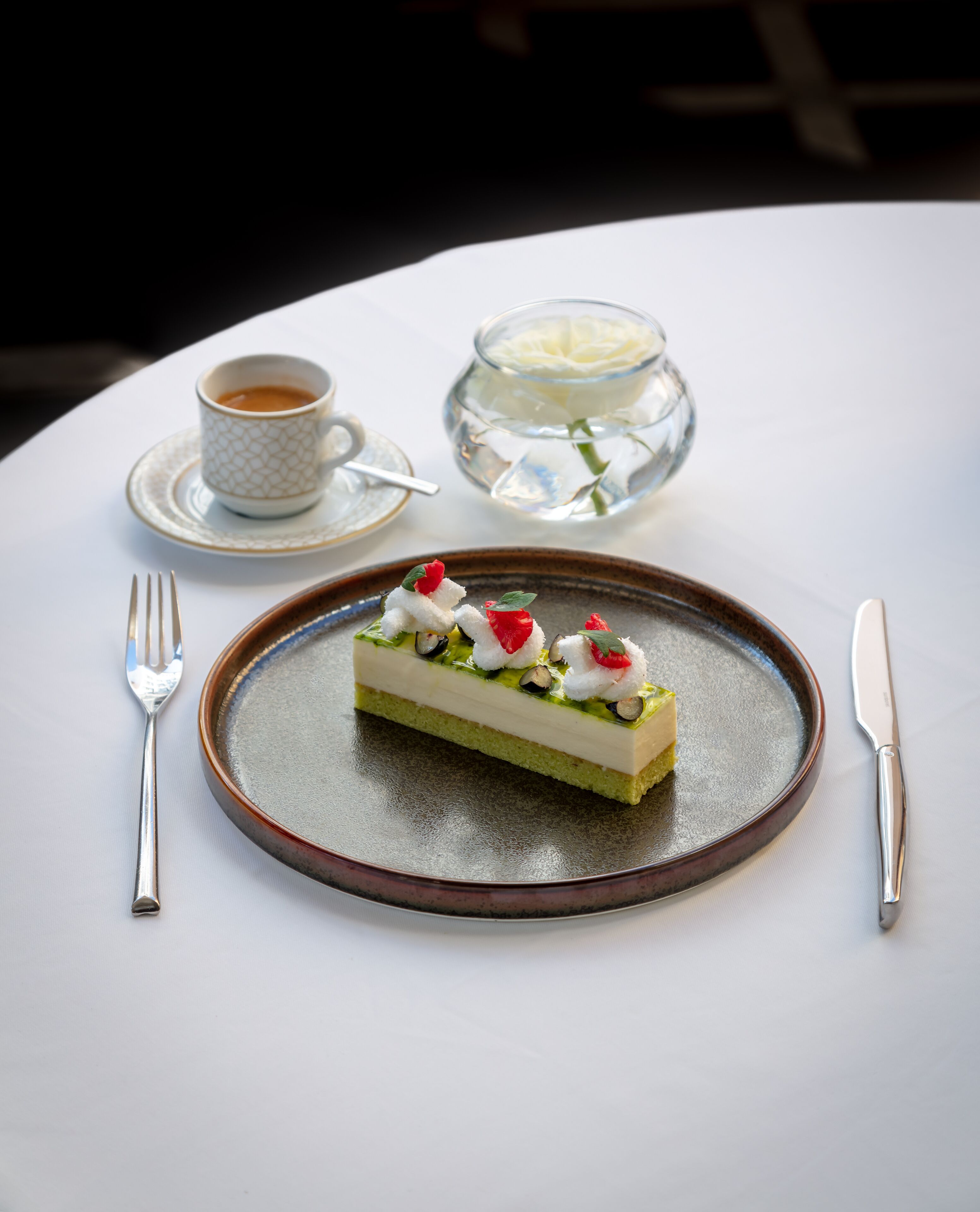 Sobremesa num prato com uma chávena de café e um copo de água sobre uma mesa.