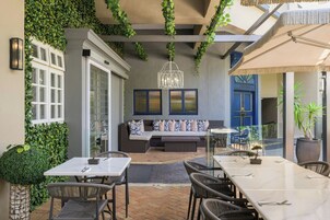 Uma área externa com mesas e cadeiras, uma porta azul e um lustre.