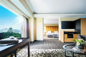 Quarto de hotel com uma cama, televisão, secretária e vista para a paisagem urbana.