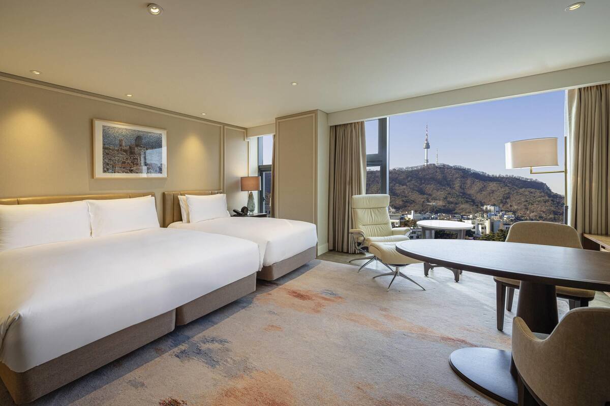 Quarto de hotel com duas camas, uma mesa de jantar e vista para a paisagem urbana.