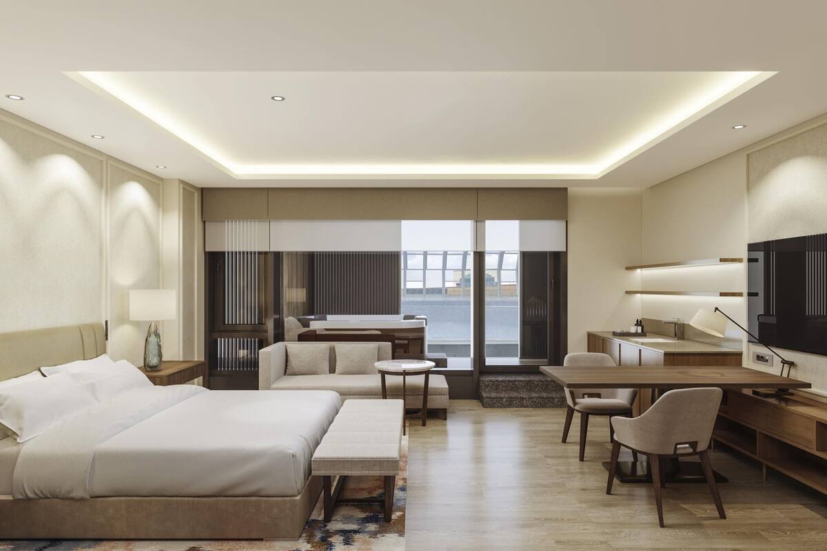 Quarto de hotel moderno com cama, área de estar, escrivaninha e uma televisão grande.