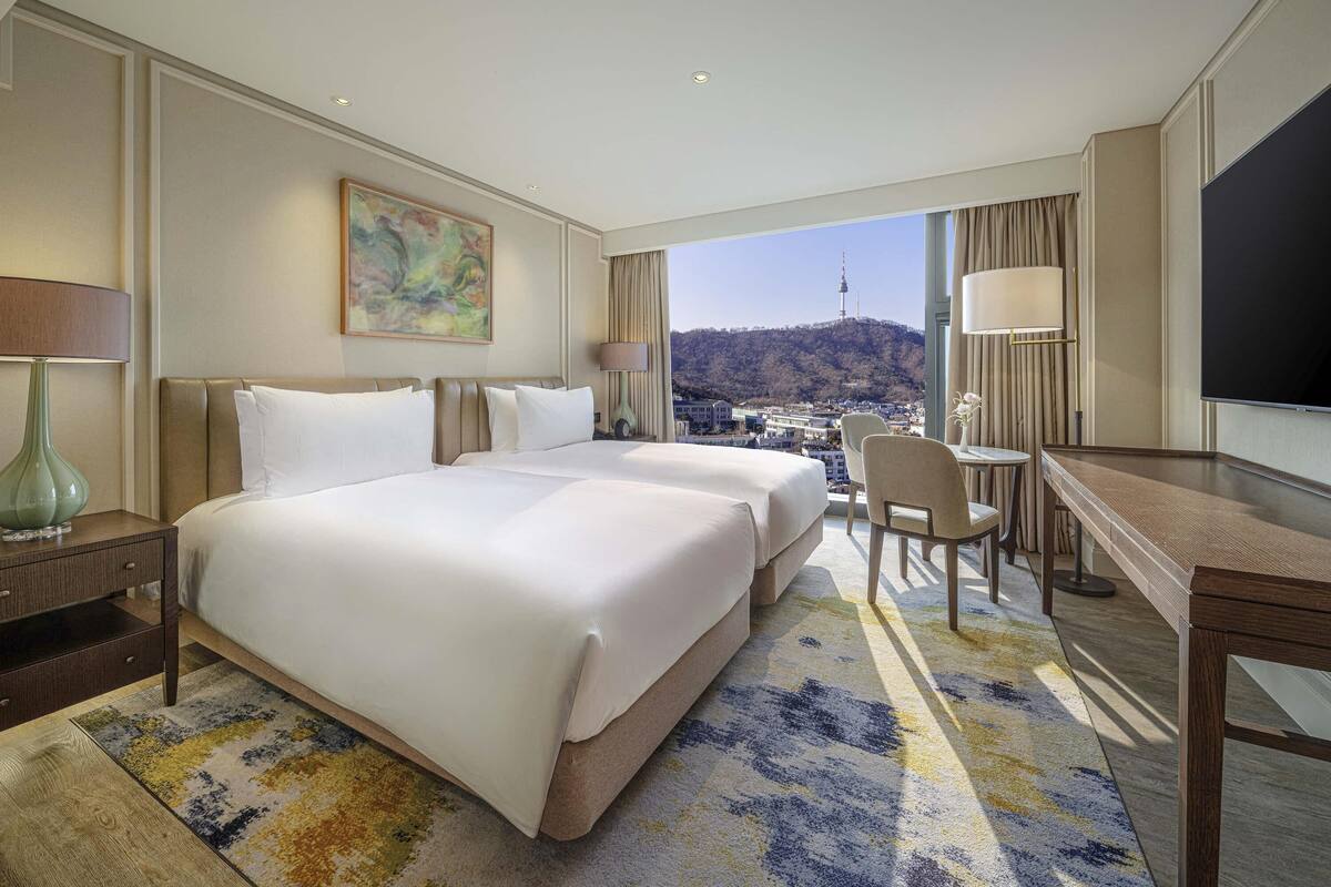 Quarto de hotel com uma cama grande, uma mesa, uma cadeira e vista para a paisagem urbana.