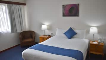 Quarto de hotel com uma cama grande, duas mesas de cabeceira com luminárias, uma cadeira, uma janela com cortinas e uma obra de arte na parede.