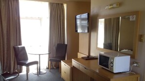 Quarto de hotel com escrivaninha, uma cadeira, televisão, micro-ondas e um espelho grande.
