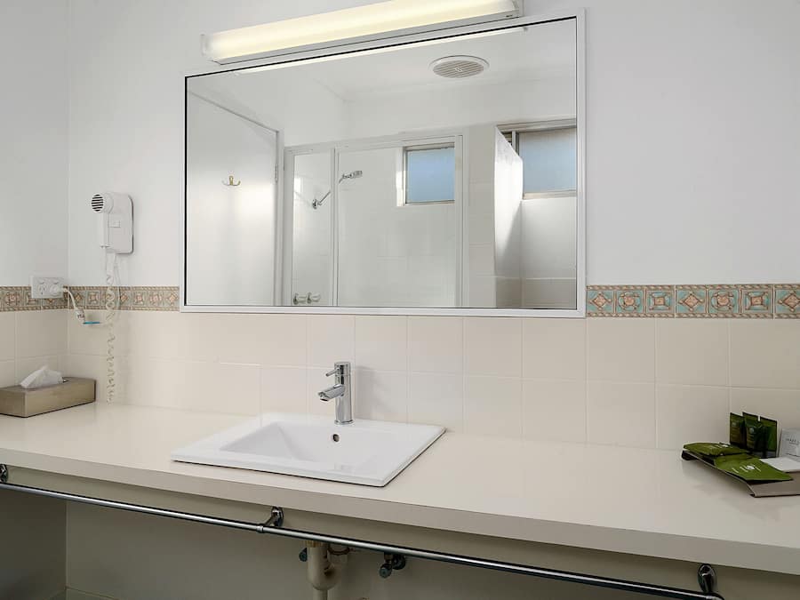 Casa de banho com lavatório branco, espelho e porta-toalhas.
