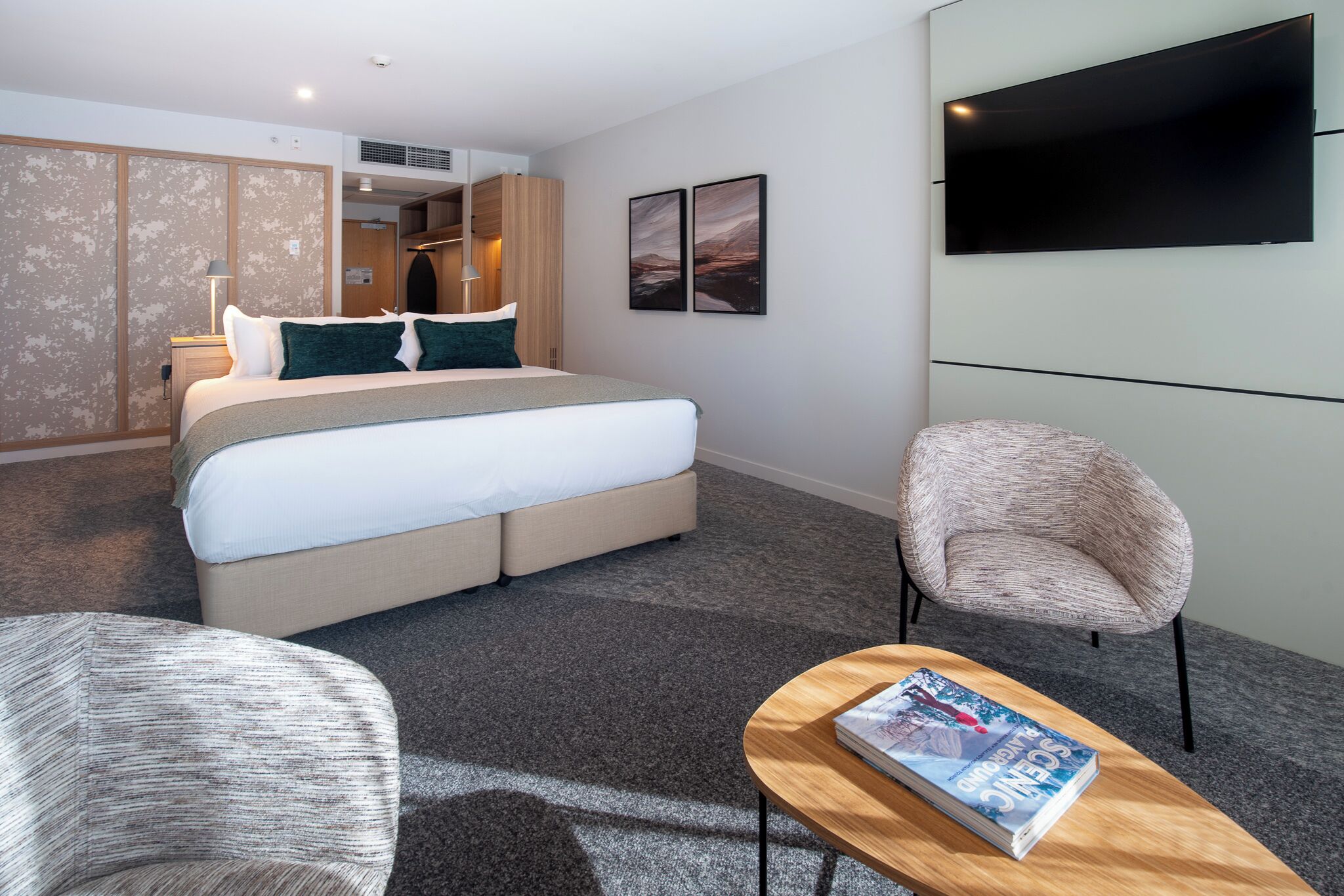 Quarto de hotel moderno com uma cama grande, televisão de tela plana e um espaço de estar com um livro.