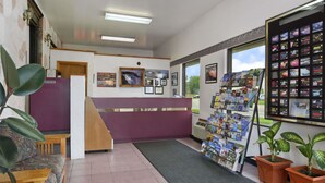 Uma área de recepção com balcão roxo, quadros nas paredes, uma janela grande e uma seleção de revistas.