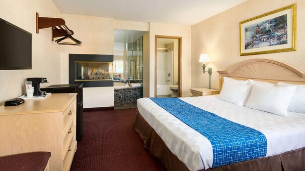 Quarto de hotel com cama, escrivaninha, penteadeira, espelho, quadro e vista para o banheiro.
