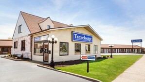 Um hotel Travelodge com placa de escritório visível, gramado bem cuidado e céu claro.