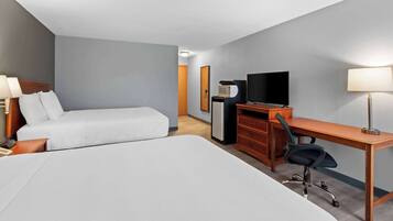 Quarto de hotel com cama, escrivaninha, cadeira, televisão e frigorífico.