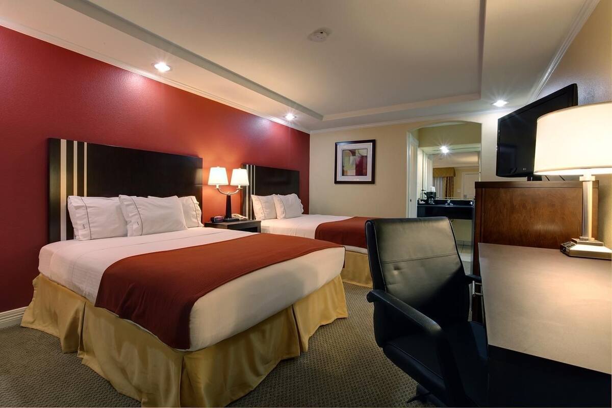 Quarto de hotel com duas camas, uma escrivaninha, uma cadeira e uma televisão.