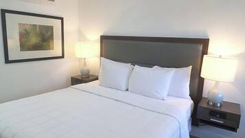 Quarto de hotel com uma cama grande, duas mesas de cabeceira com luminárias, ar condicionado fixado na parede e um quadro emoldurado.