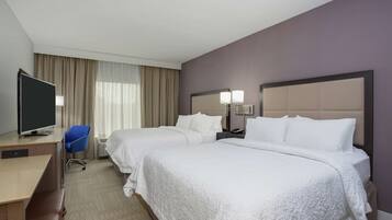 Quarto de hotel com duas camas, uma mesa, uma televisão e uma cadeira.